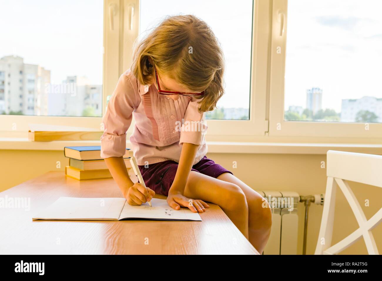 Schoolgirl, girl of 8 years, sitting at table with books and writing in ...