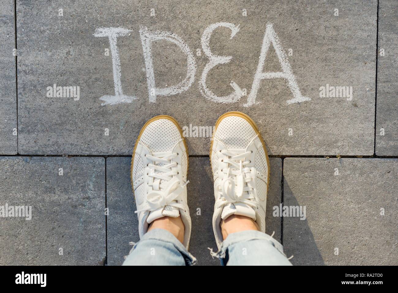 View from above, female feet with text idea written on grey sidewalk ...