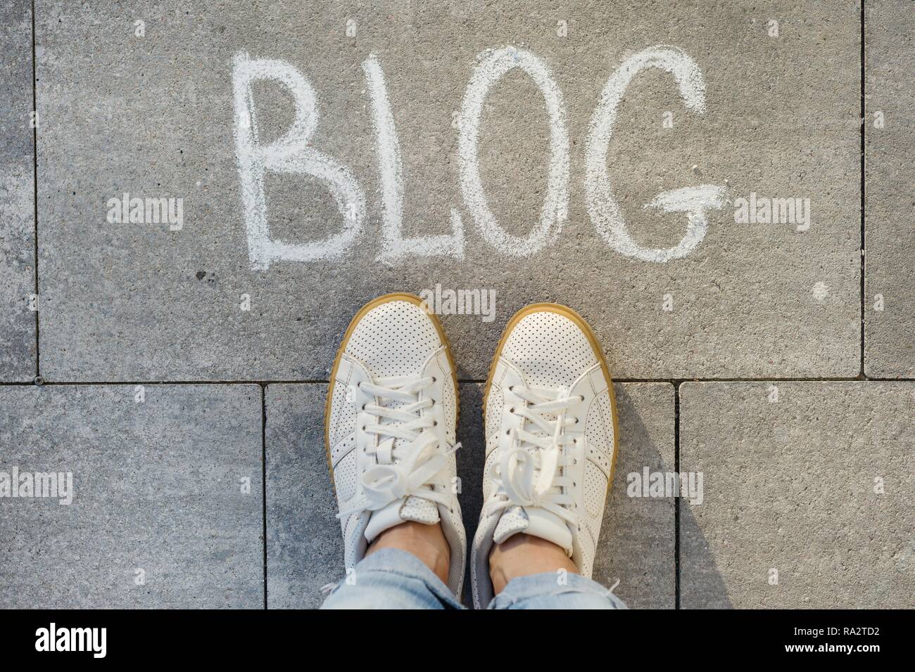 View from above, female feet with text blog written on grey sidewalk ...