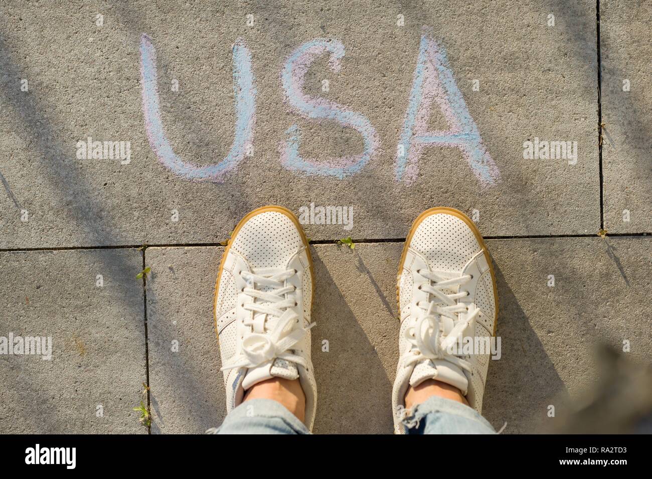 View from above, female feet with text USA written on grey sidewalk ...
