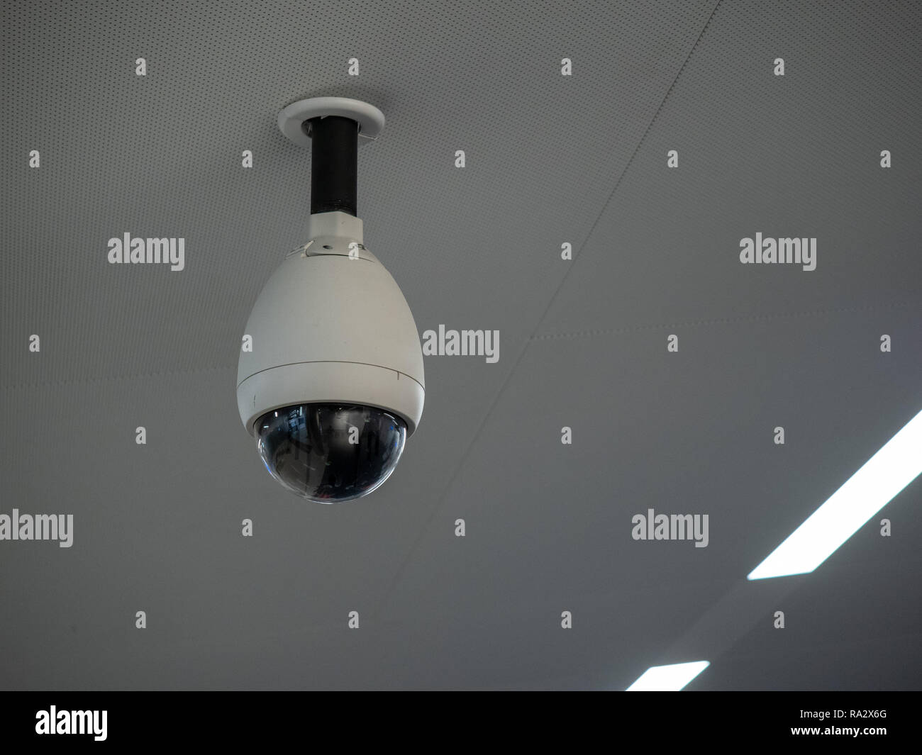 White circular surveillance camera on ceiling in a public setting ...