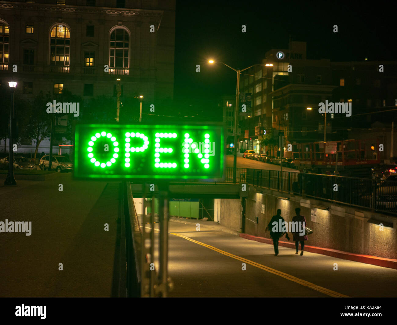 Green lighted open sign in dark city area with people walking in to ...