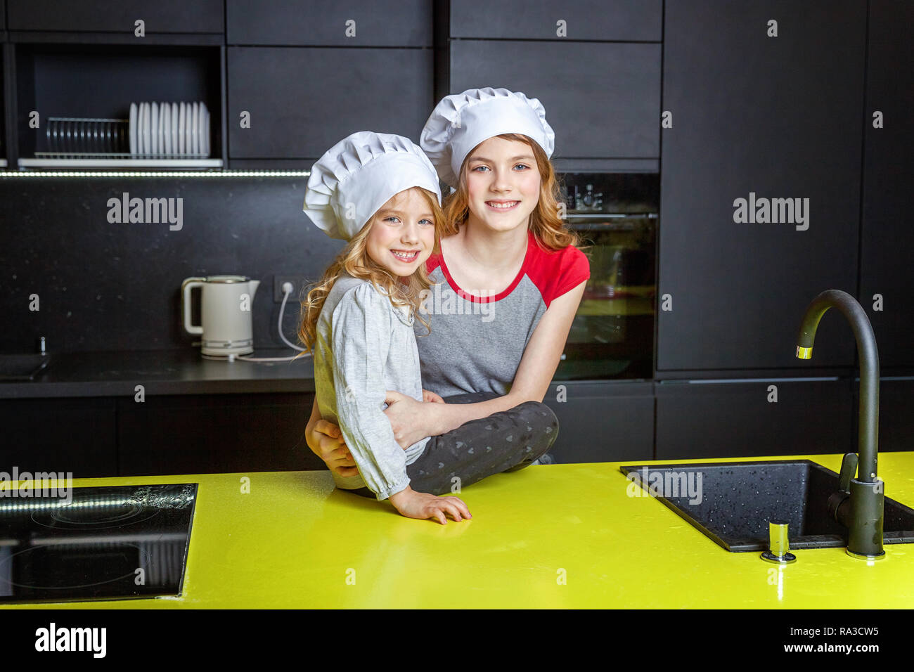 Two girls with chef hat hugging and having fun in kitchen. Sisters ...