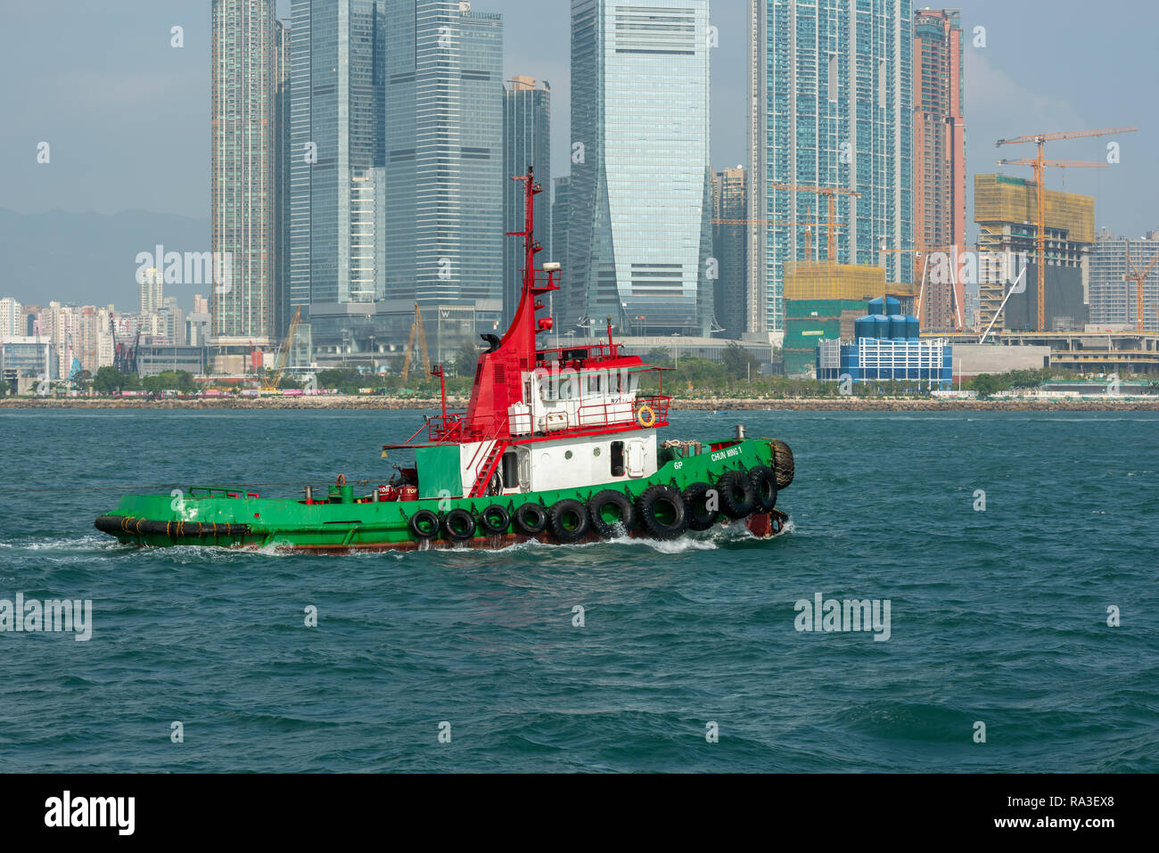 A colourful tug boat in Victoria Harbour, Hong Kong, with the towering ...