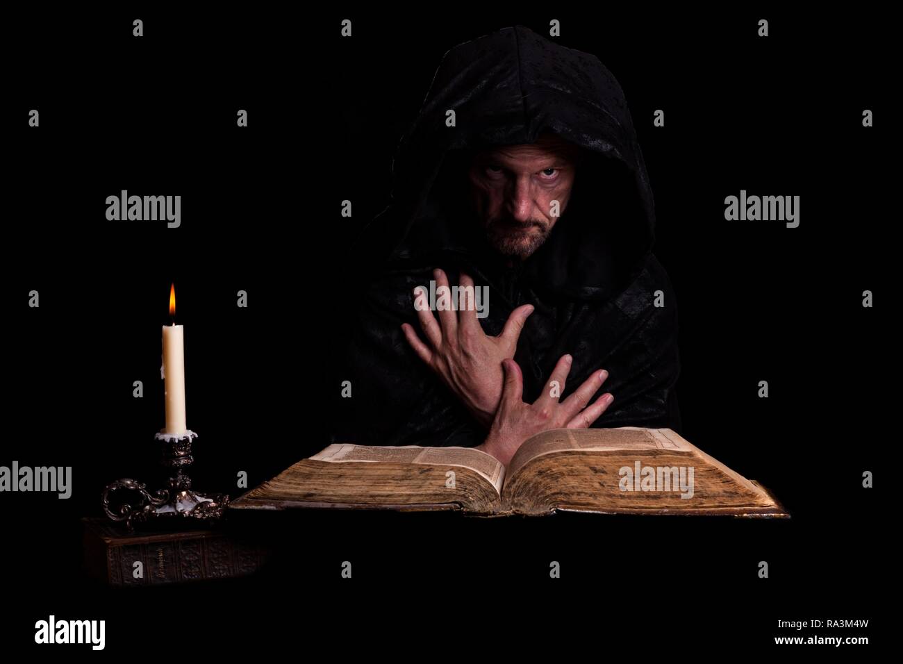 Man, with a black hooded coat, in front a burning candle and an old ...