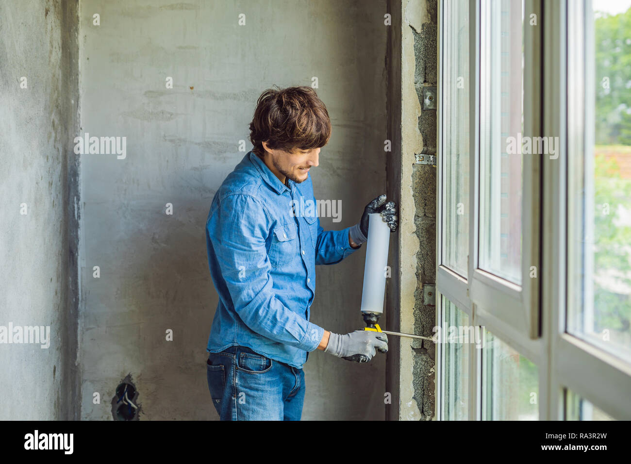 Man in a blue shirt does window installation. Using a mounting foam ...