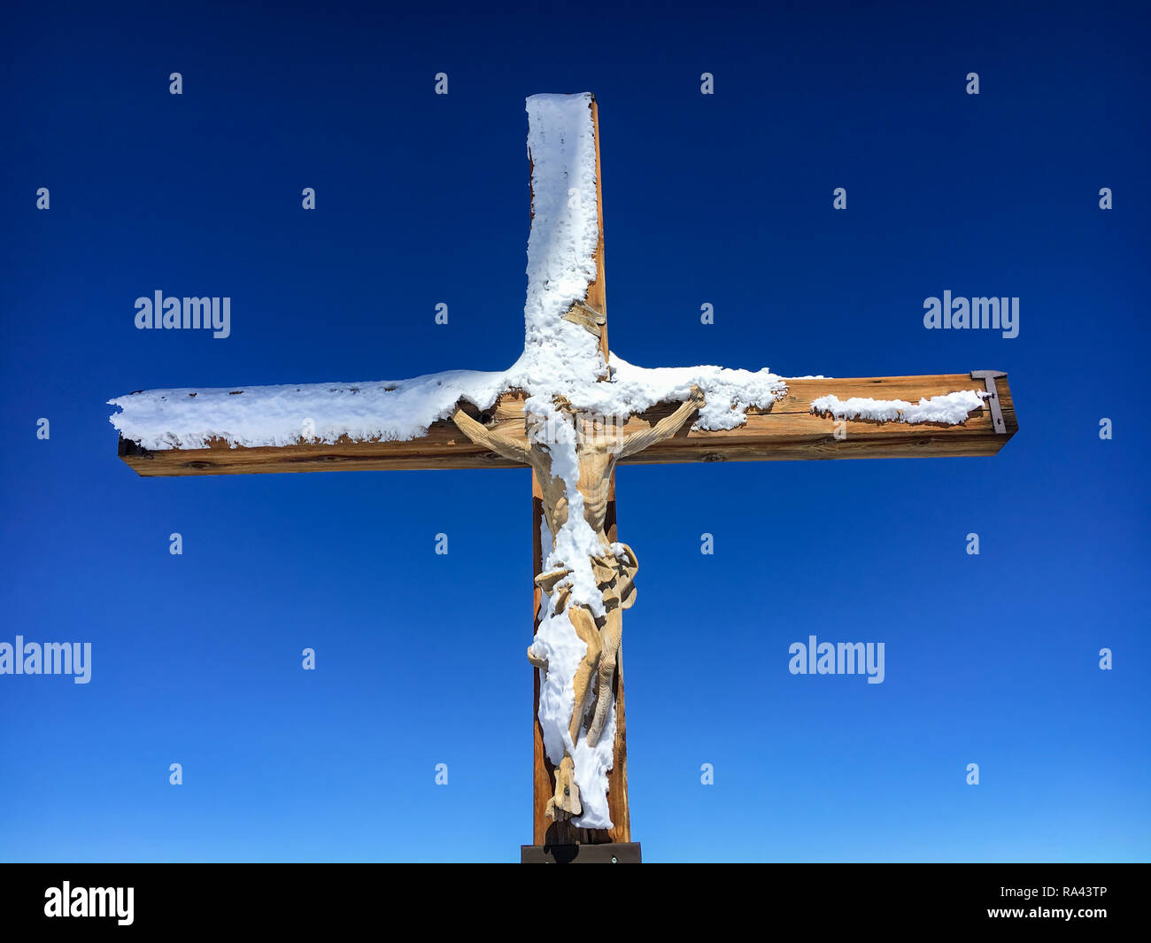 Snow covered cross with a wooden figure of Jesus Christ at peak of ...