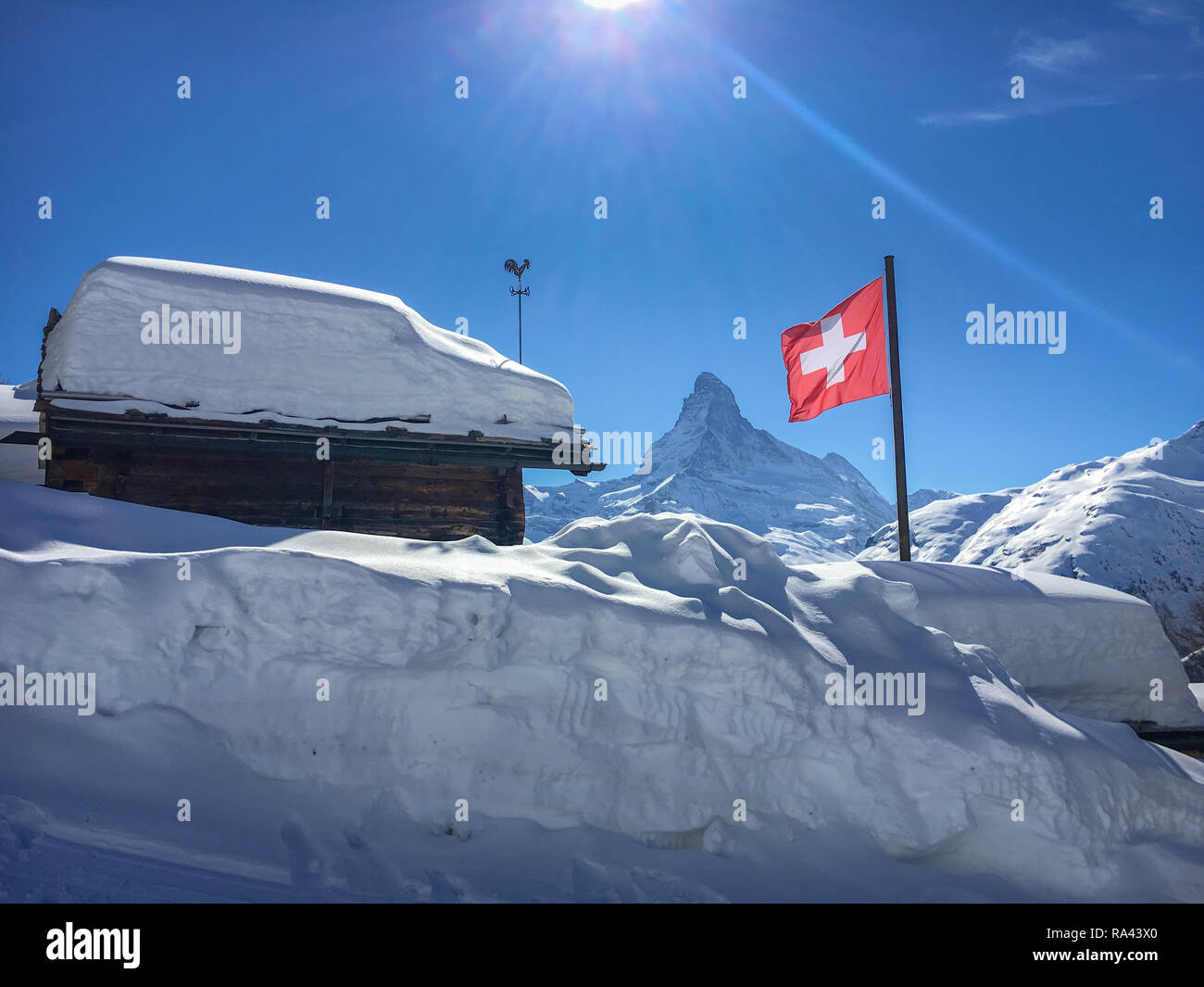 Cottage with lots of snow on the rooftop and Swiss flag in front of ...