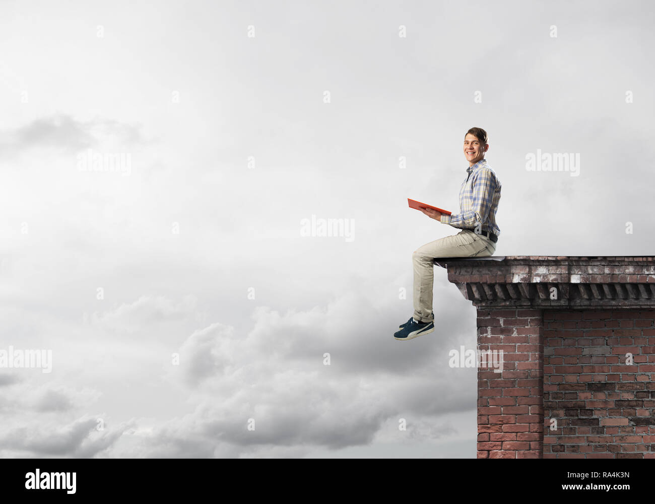 Man on roof edge reading book and cloudscape at background Stock Photo ...
