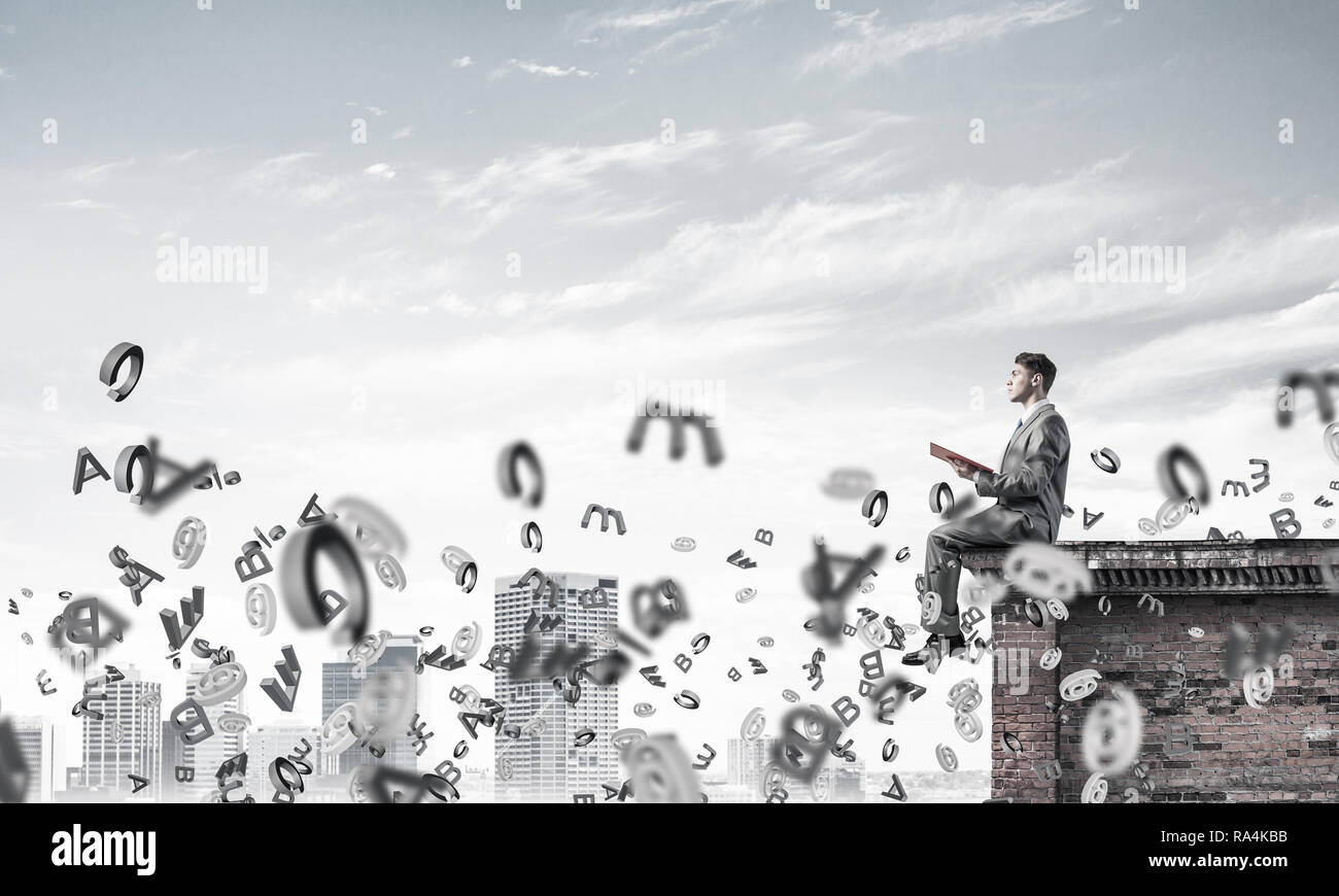 Man on roof edge reading book and symbols flying around Stock Photo - Alamy