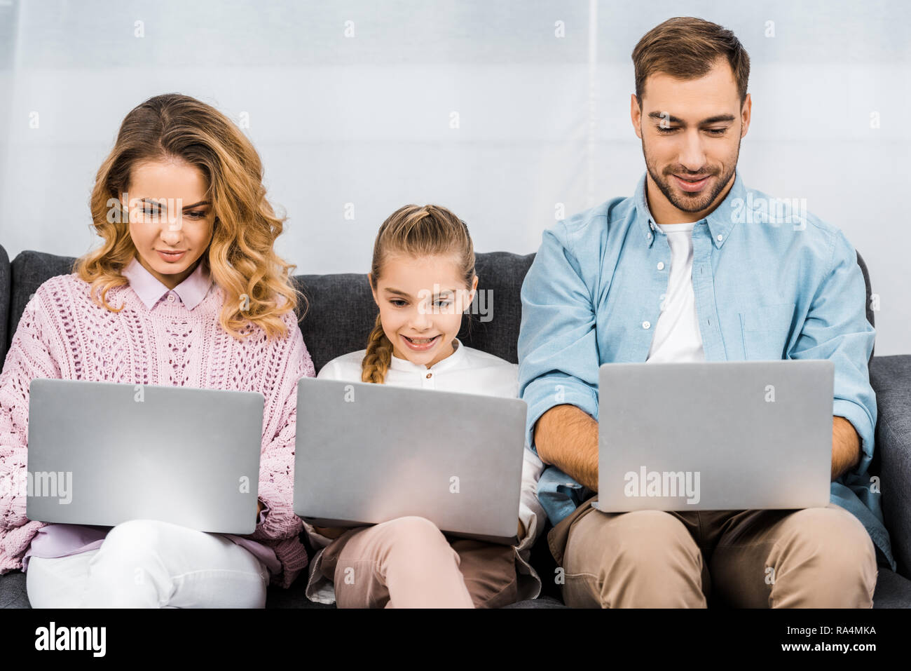 cute girl with two parents using laptops and sitting on sofa in living ...