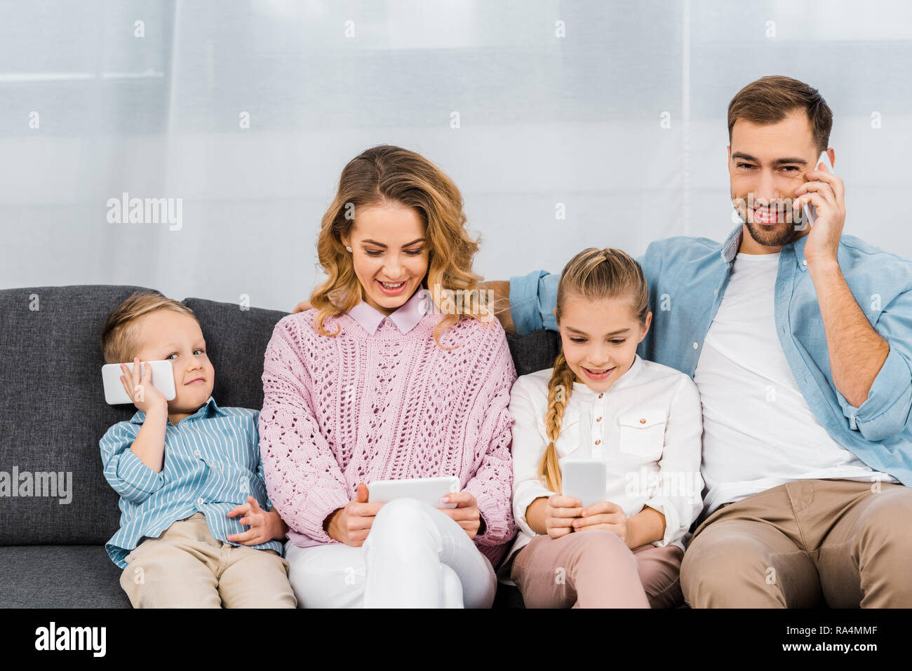 smiling father sitting on sofa and talking on phone while mother and ...