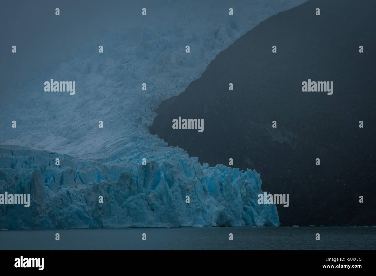 Blue ice of Patagonian glacier and dark rock in moody day, viewed ...