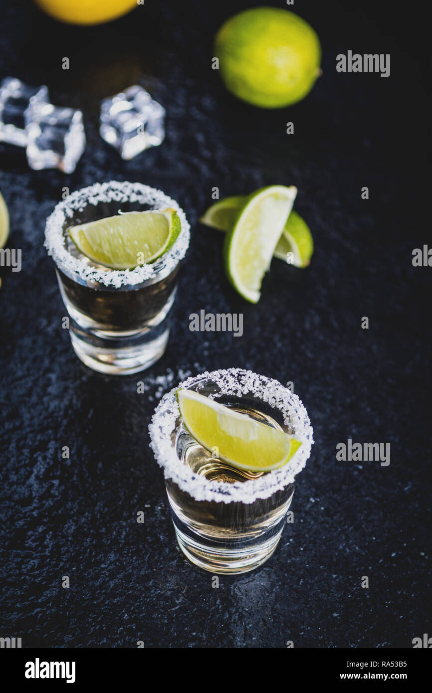 Mexican traditional Tequila with lemon, lime,salt and ice cube on dark ...