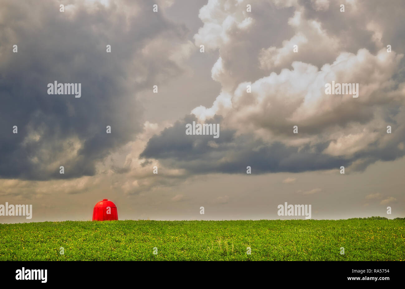 One red plastic hut on a green field under a cloudy threatening sky in ...
