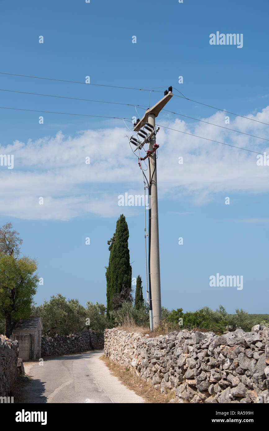 Tall concrete pole with electric wire in countryside. Narrow road with ...