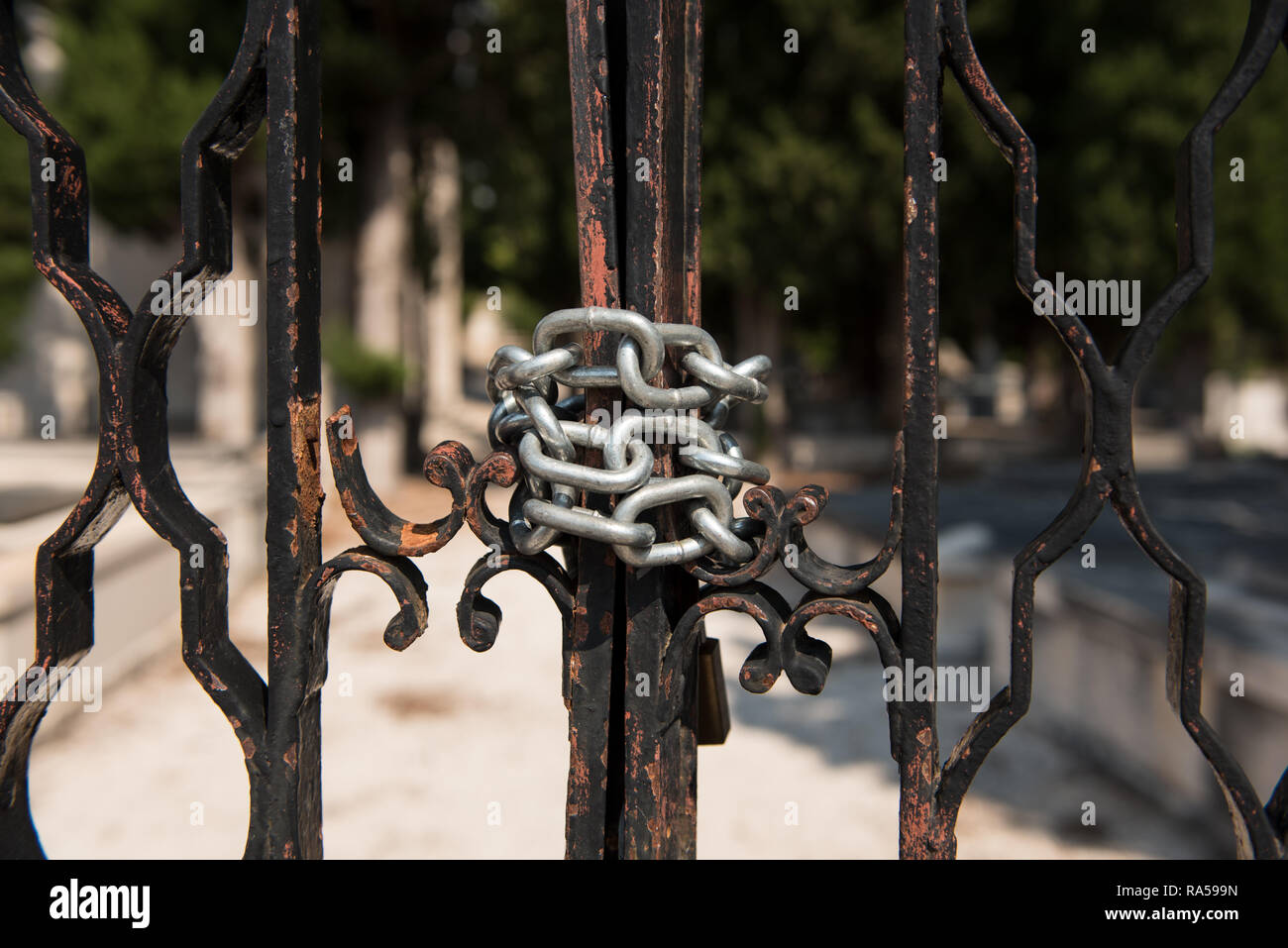 Silver chain on a metal graveyard fence. Closed old metal doors with ...