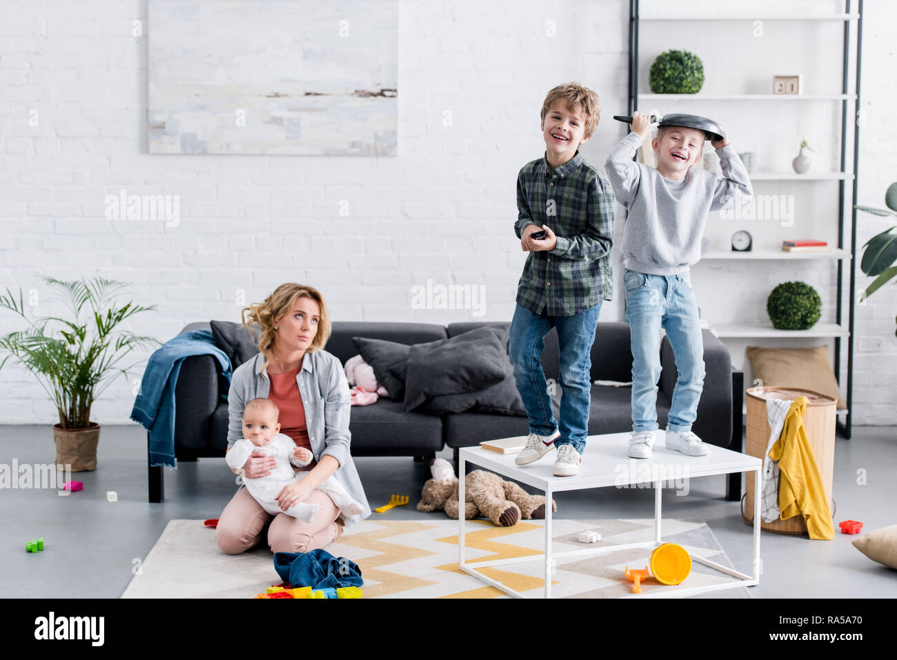 exhausted mother holding infant child while naughty kids playing at ...