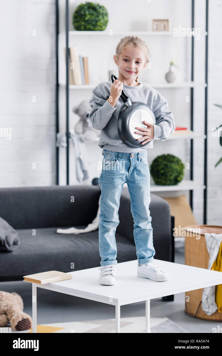 happy child standing on table and playing with frying pan at home Stock ...