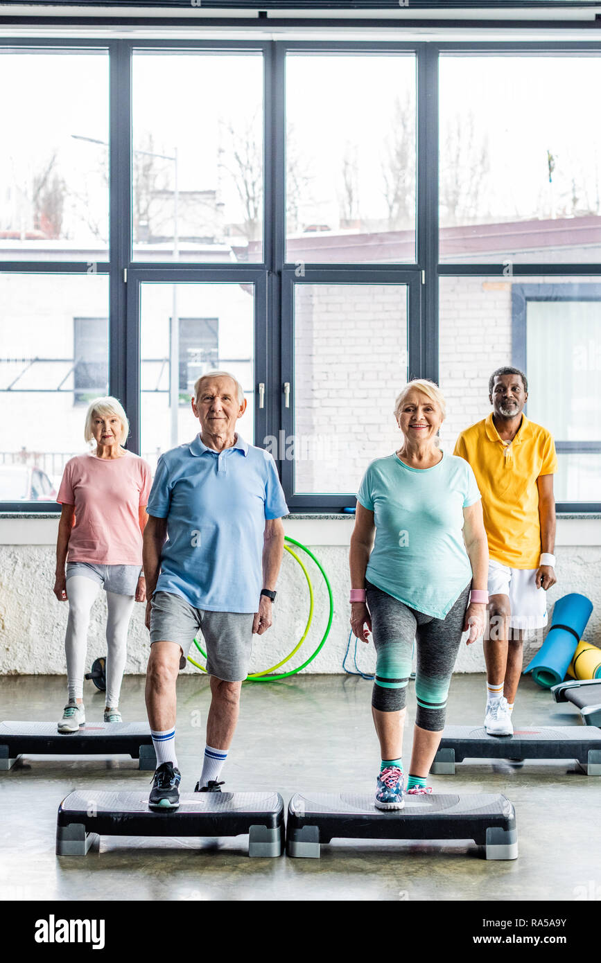 happy multicultural senior athletes synchronous exercising on step ...