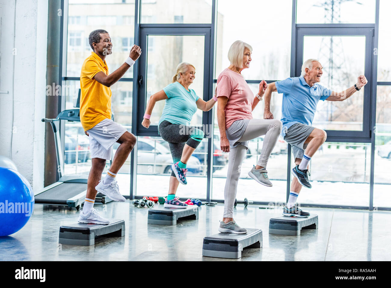 side view of multiethnic senior athletes synchronous exercising on step ...