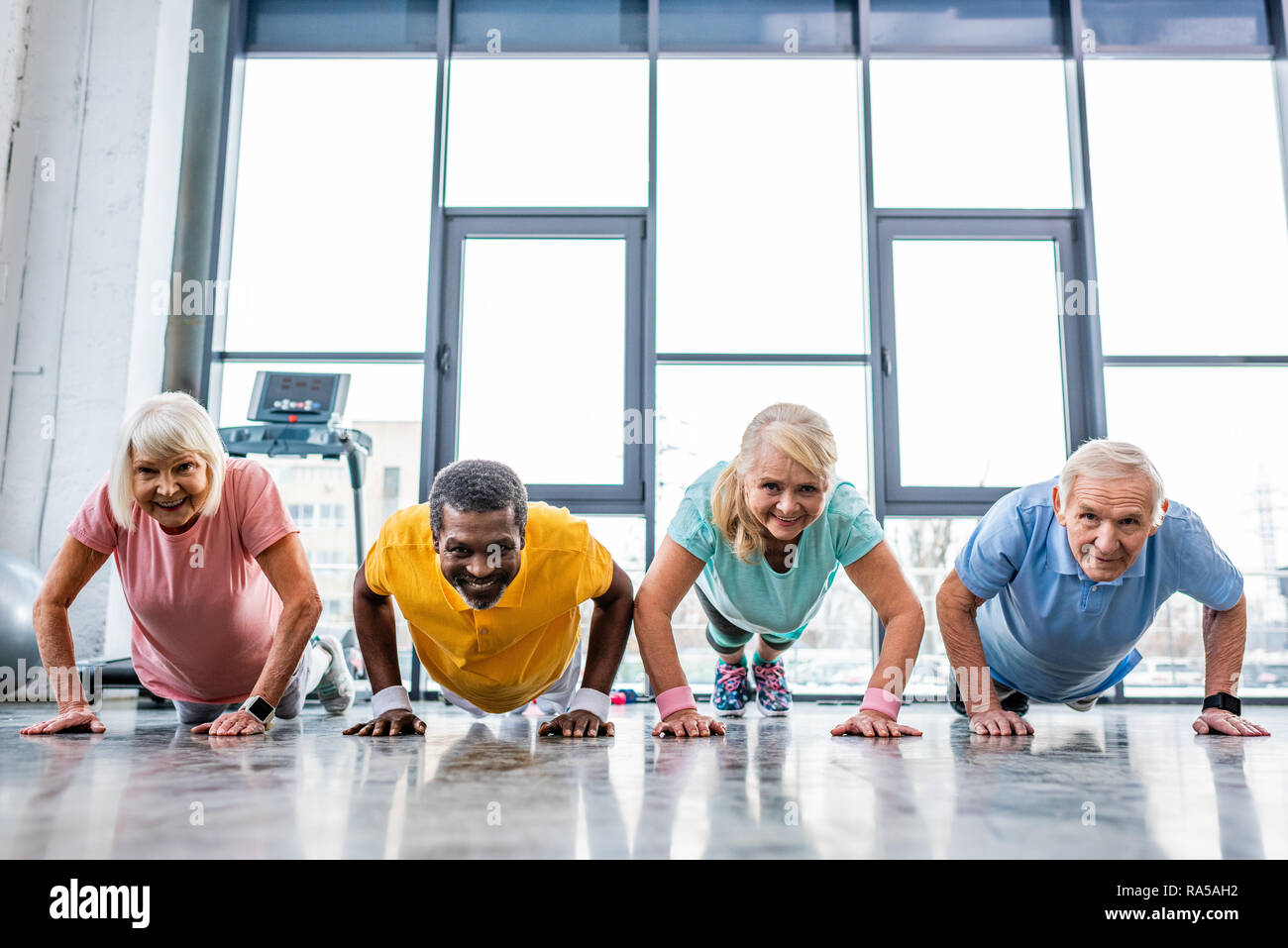 smiling multiethnic senior sportspeople synchronous doing plank at gym ...