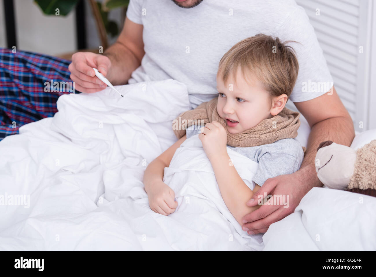 cropped image of dad hugging sick son in bedroom and checking his ...