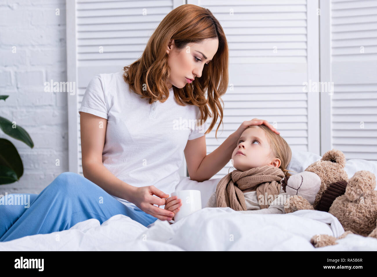 mother taking care of sick daughter in bedroom and giving her cup of tea, looking at each other ...