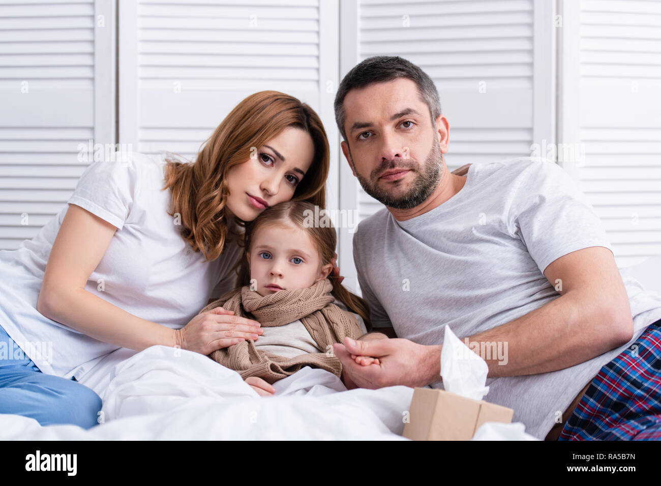 parents taking care of sick daughter in bedroom and looking at camera ...