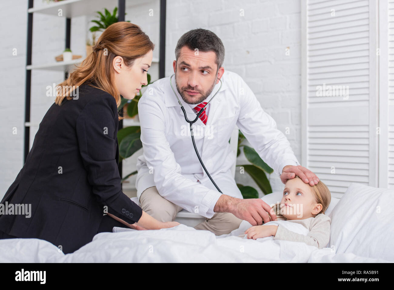 pediatrist in white coat examining sick kid with stethoscope at home ...