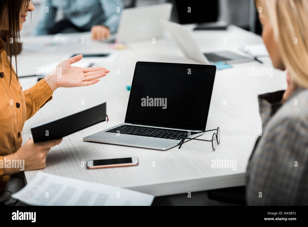 partial view of businesswomen working on project together at workplace ...