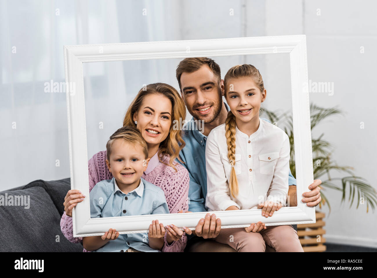 happy family holding white frame and looking at camera in living room ...