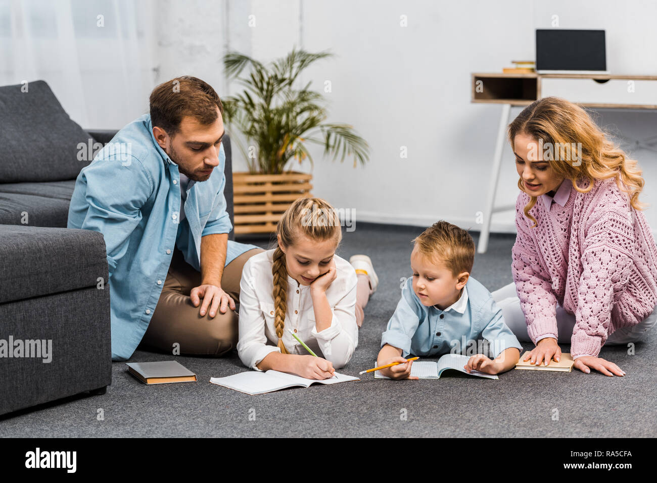 parents looking at girl and boy lying on floor and writing in exercise ...