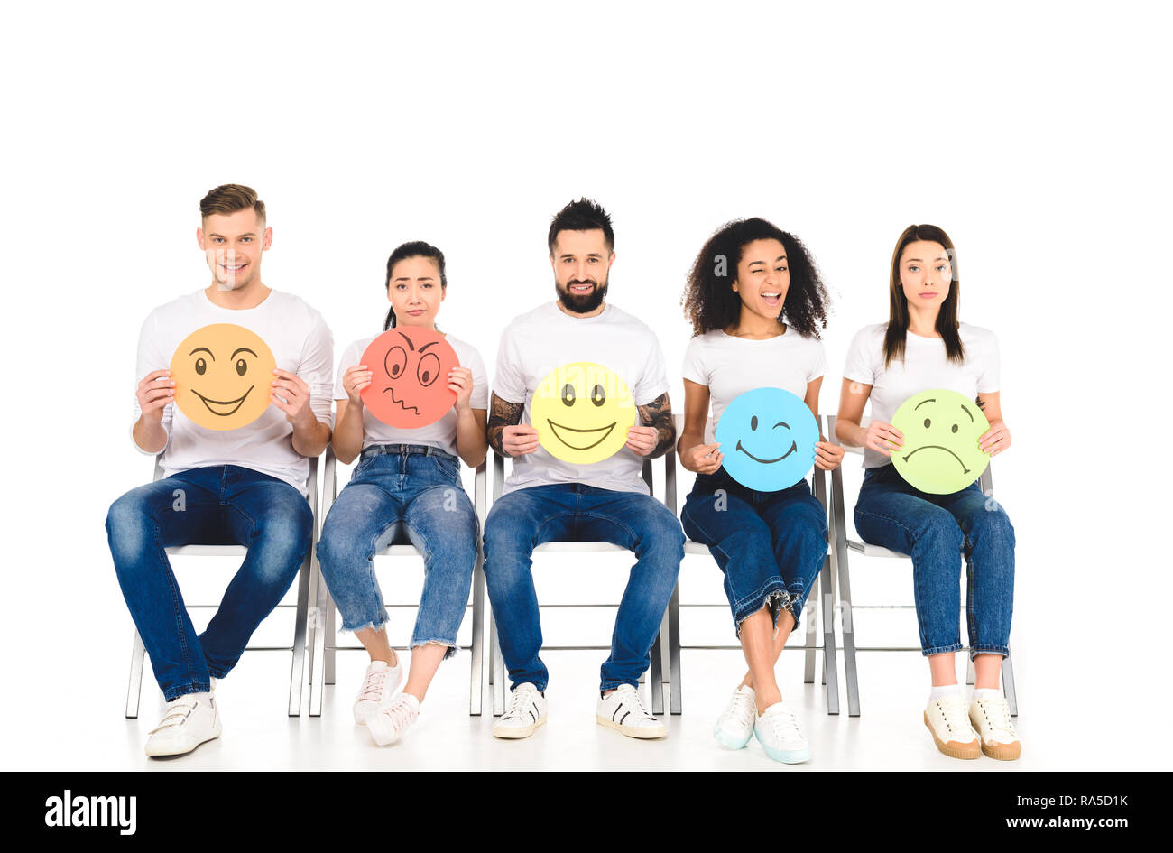 multicultural friends in blue jeans sitting on chairs and holding signs ...