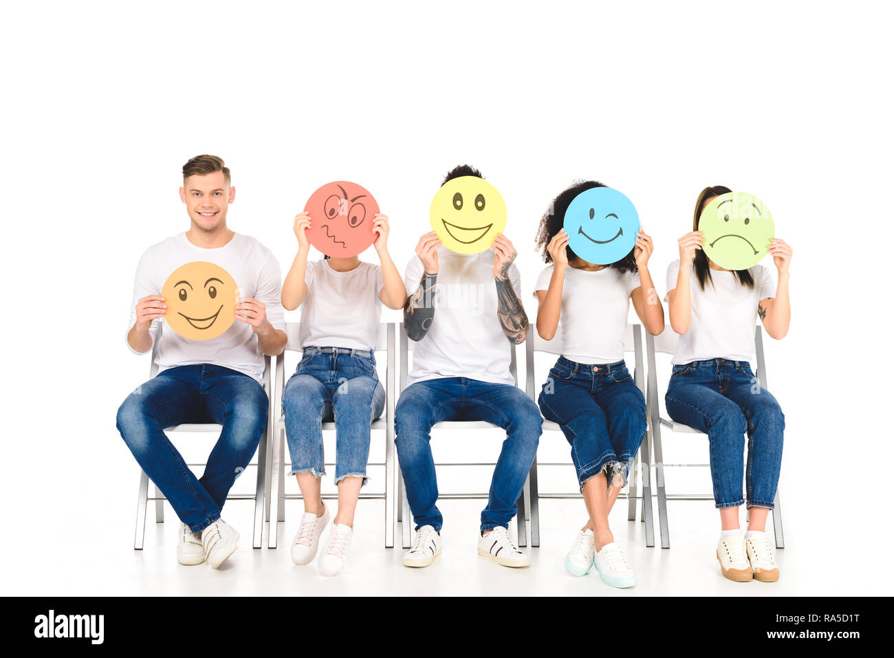 multiethnic friends in white t-shirts sitting on chairs and holding ...