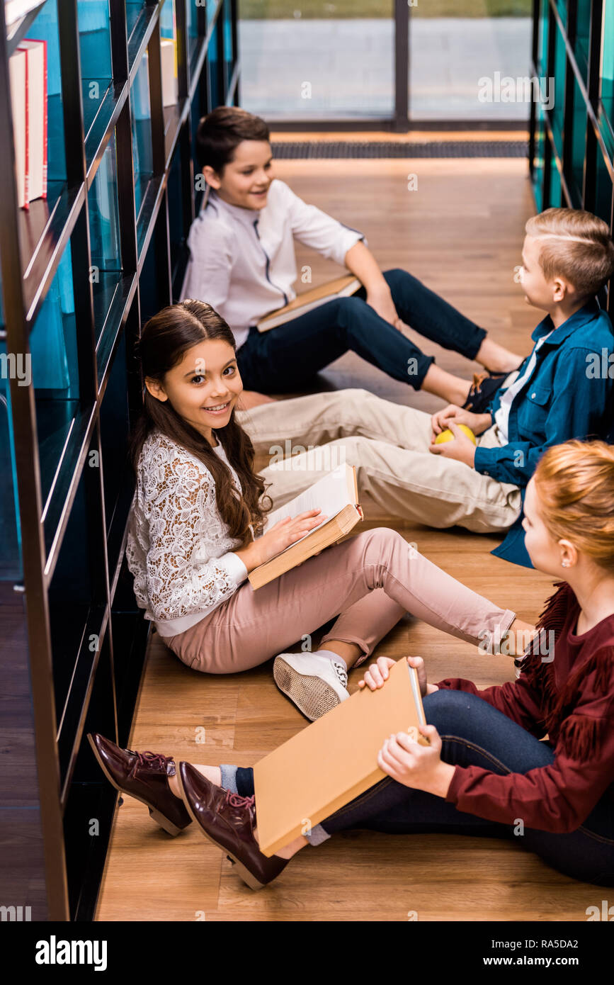 high angle view of four classmates sitting on floor and reading books ...