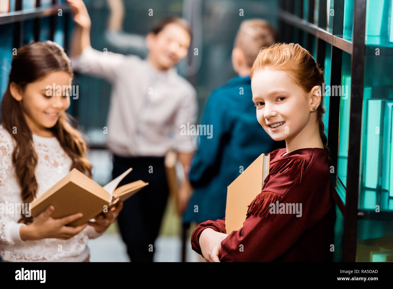 beautiful schoolchild holding book and smiling at camera while visiting ...