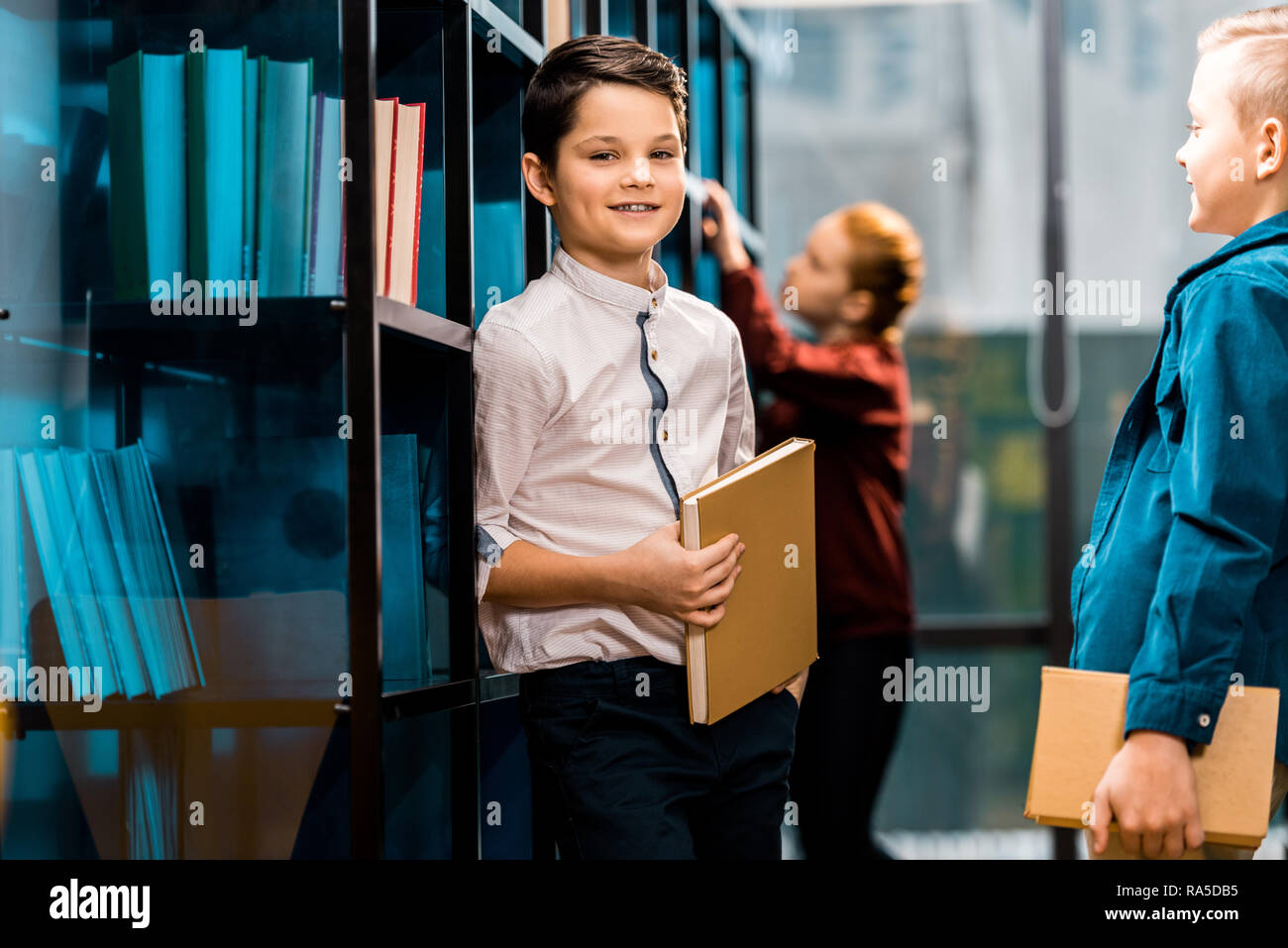 cute smiling schoolchildren holding books while studying in library ...
