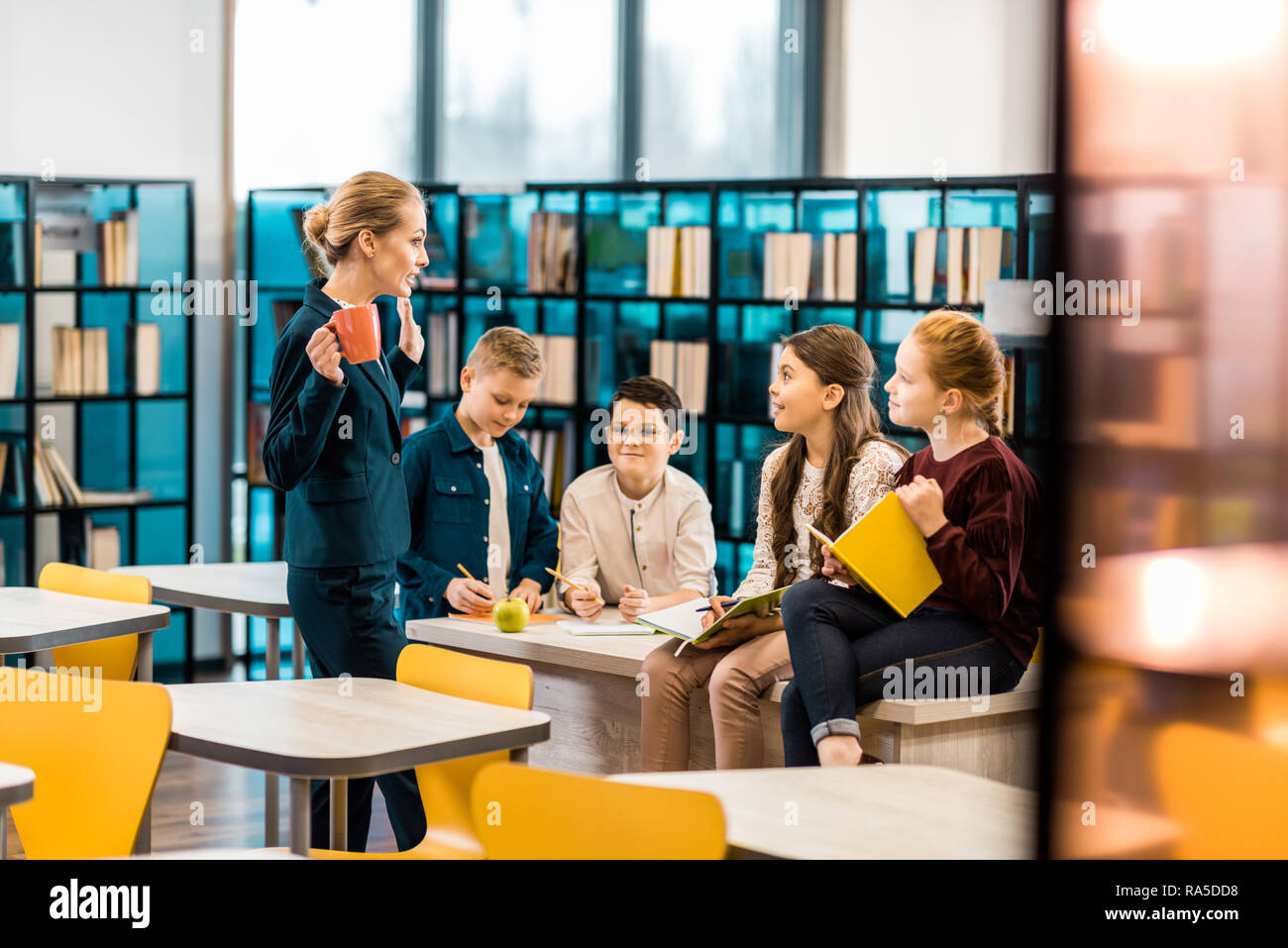 young female librarian and schoolkids talking together in library Stock ...