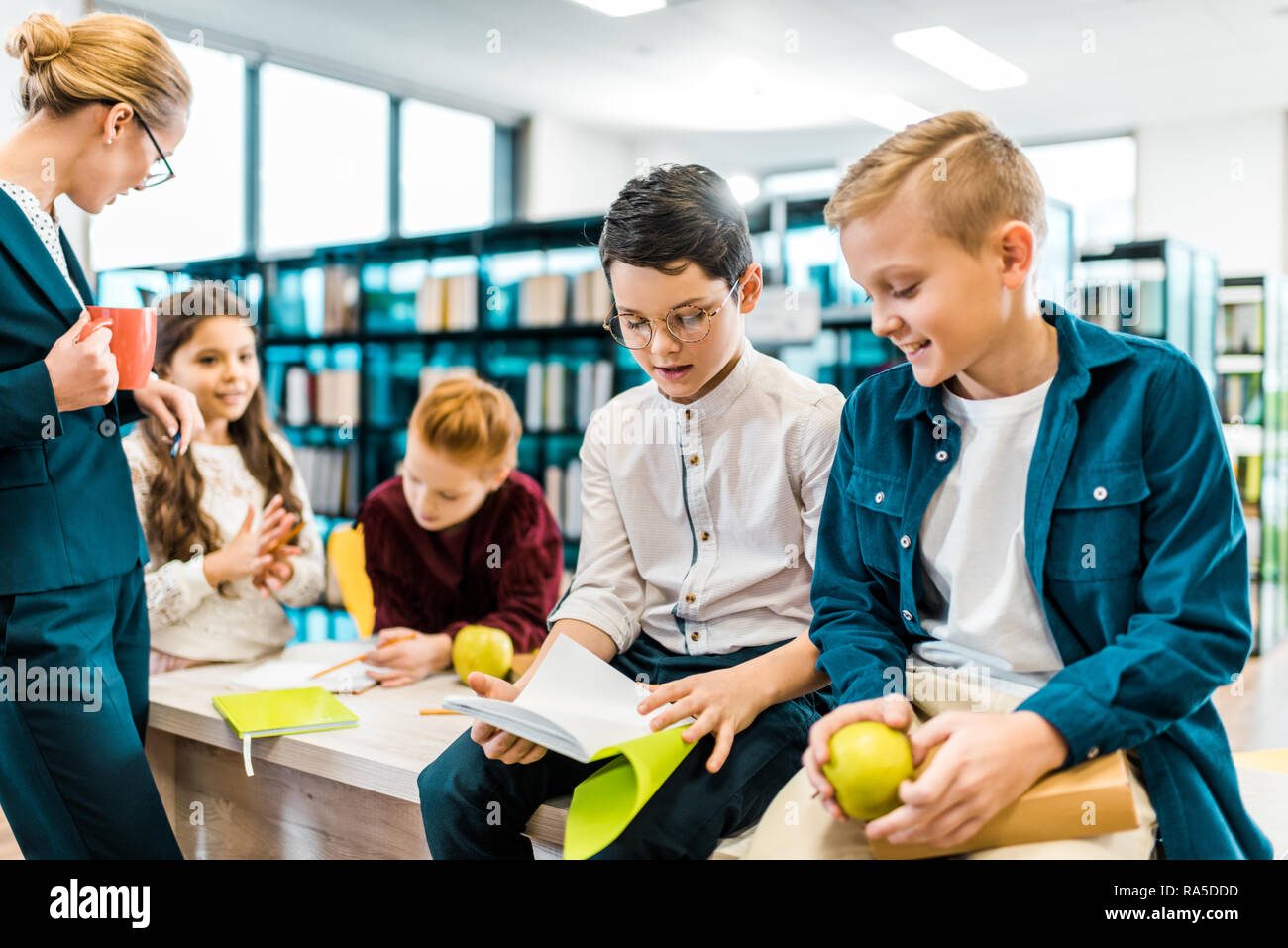 young female librarian looking at kids reading books in library Stock ...