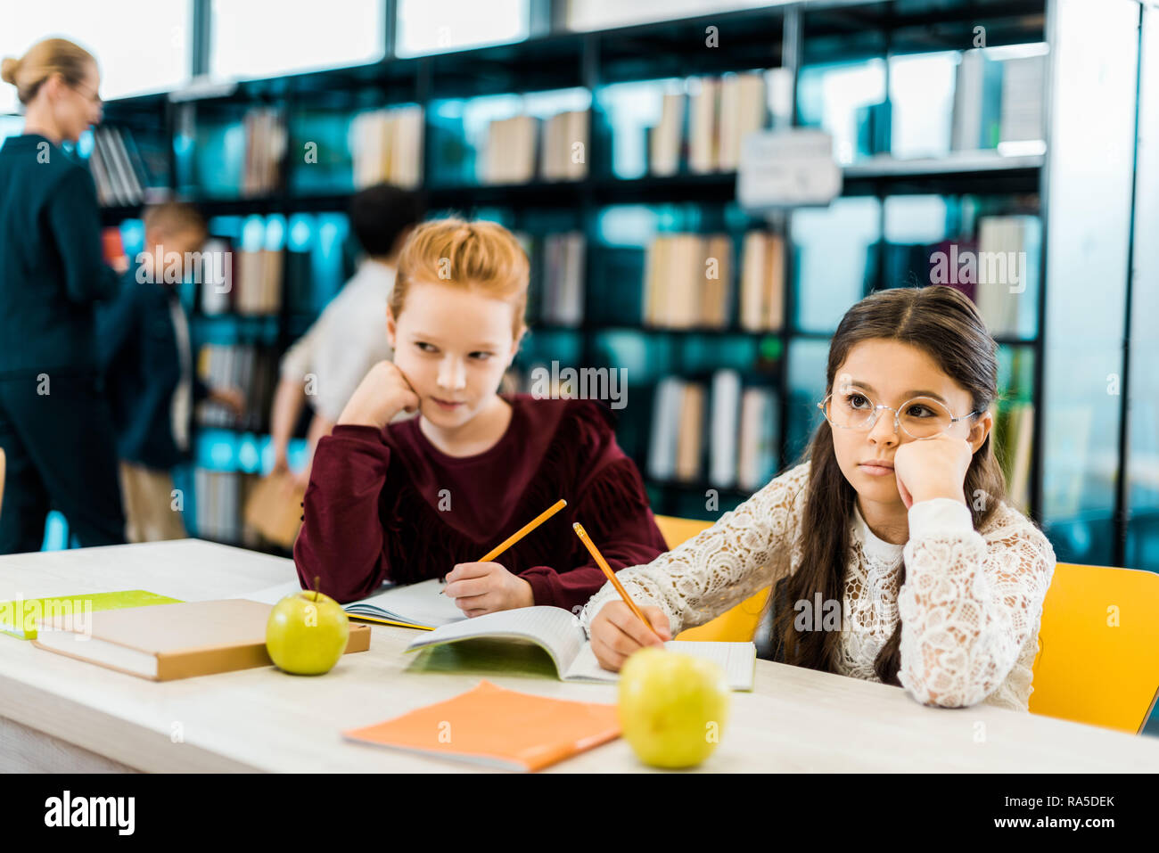 schoolkids writing with pencils and looking away in library Stock Photo ...