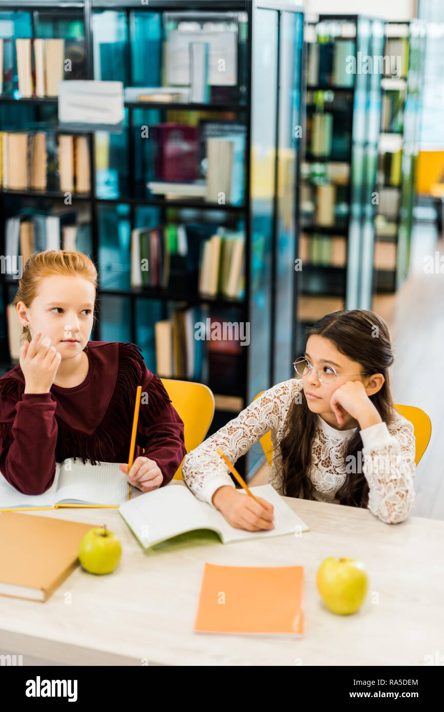 schoolgirls writing with pencils while studying in library Stock Photo ...