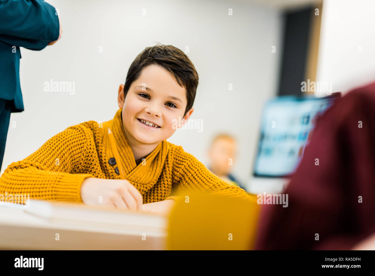 adorable schoolkid writing with pencil and smiling at camera Stock ...