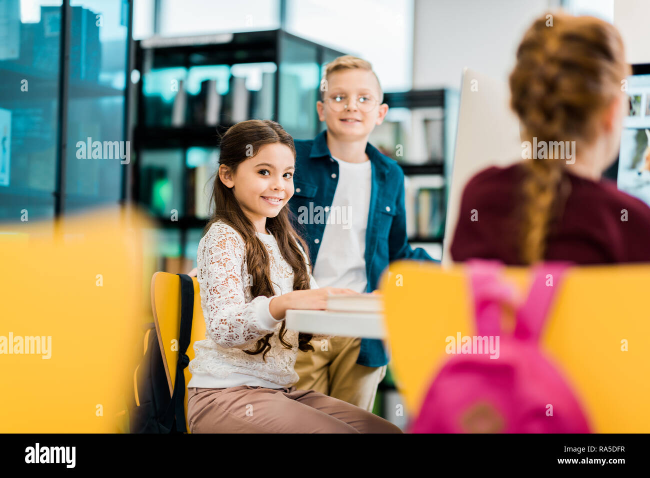 cute smiling schoolchildren studying with desktop computers in library ...