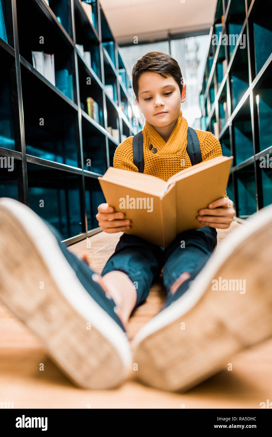 schoolboy sitting on floor and reading book in library Stock Photo - Alamy
