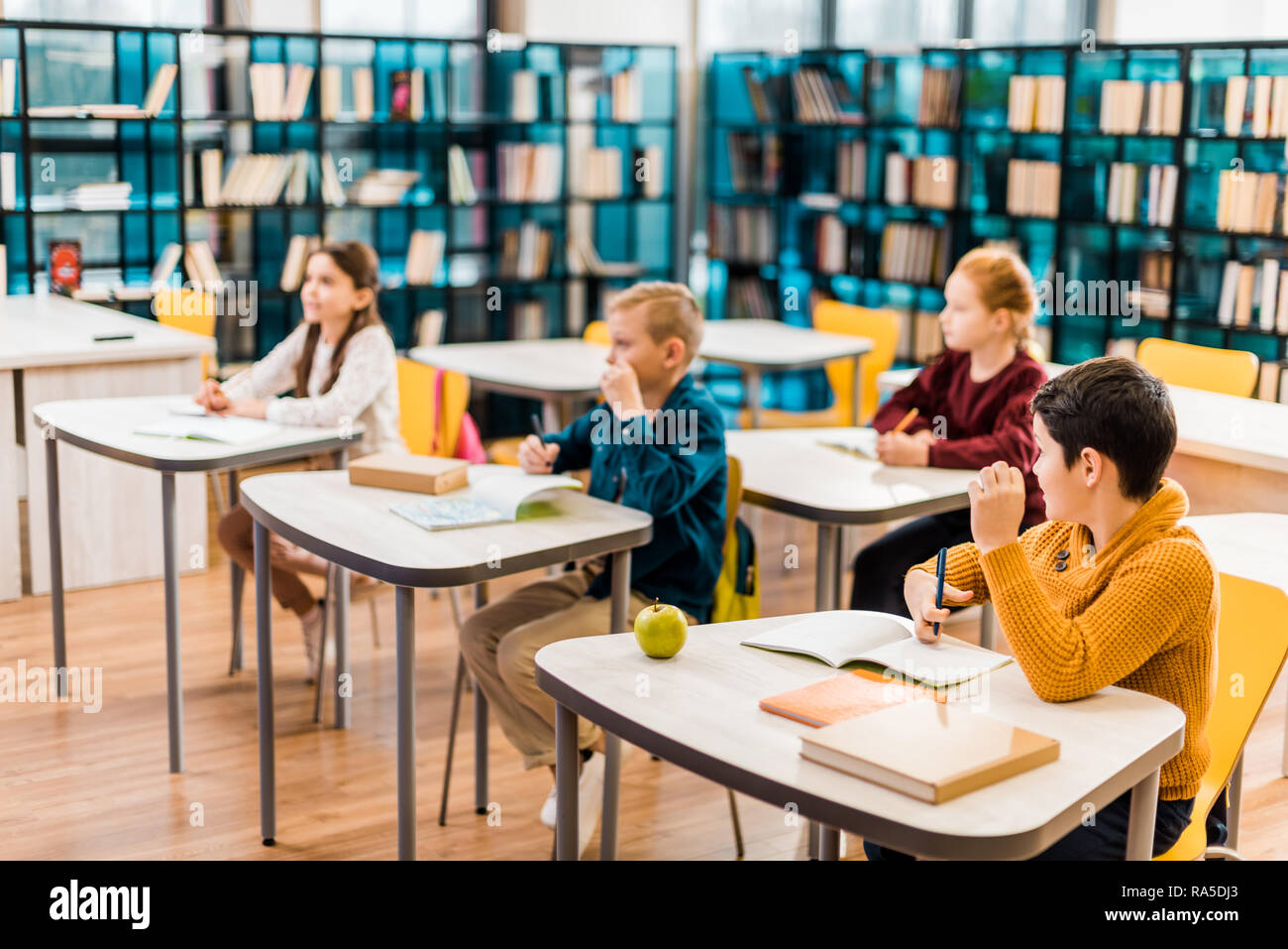 children sitting at desks and looking away during lesson in library ...