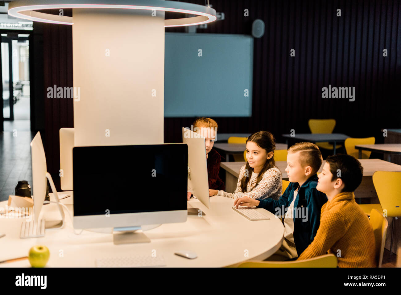 adorable schoolchildren sitting and using desktop computer together in ...