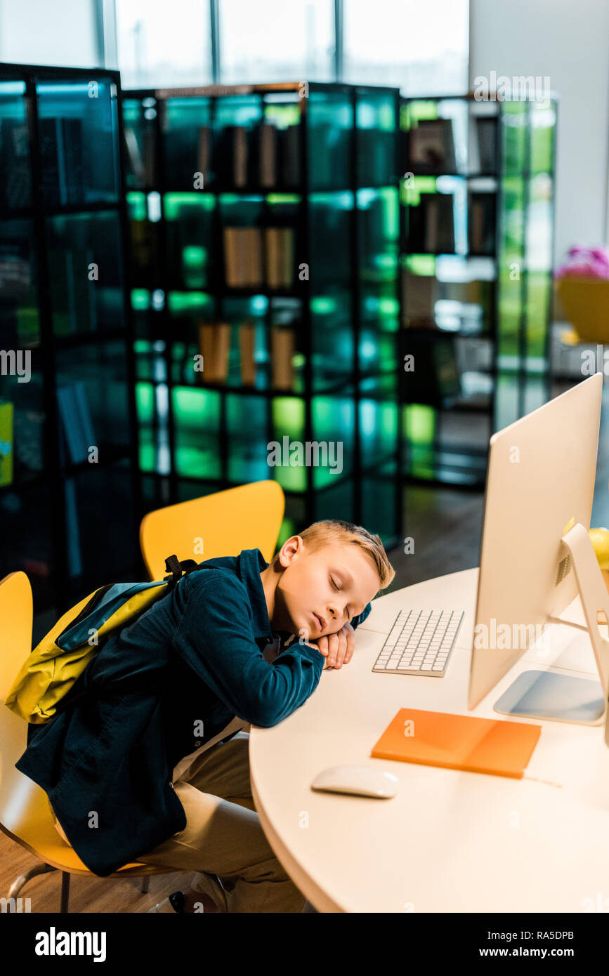 high angle view of schoolboy with backpack sleeping on desk with ...