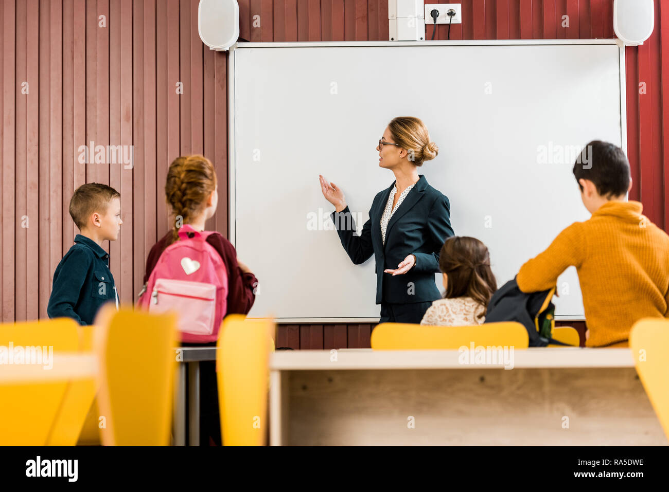 back view of schoolkids with backpacks looking at teacher making ...