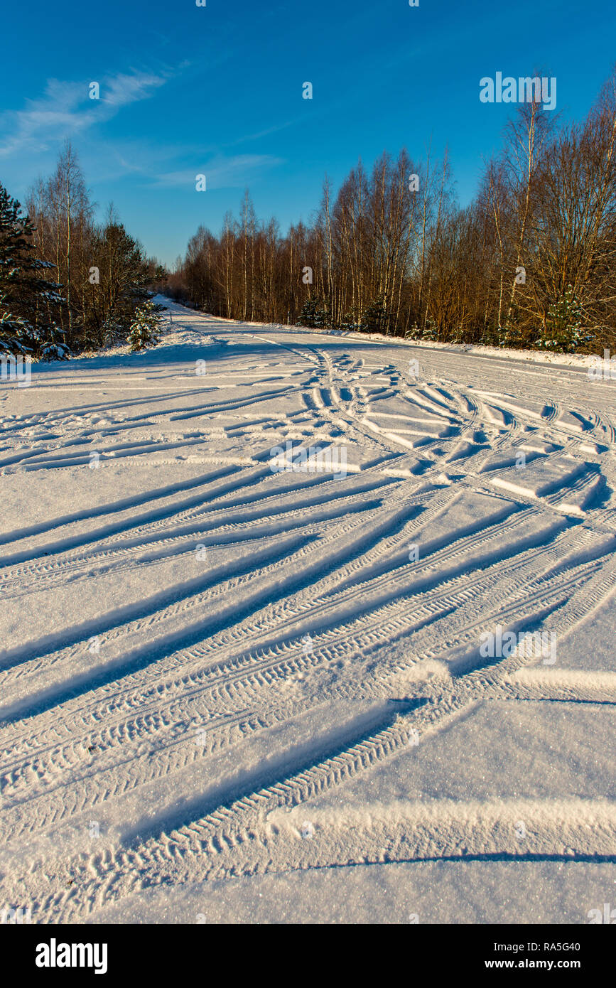 snow covered winter road with tire tracks in perspective with blue sky ...